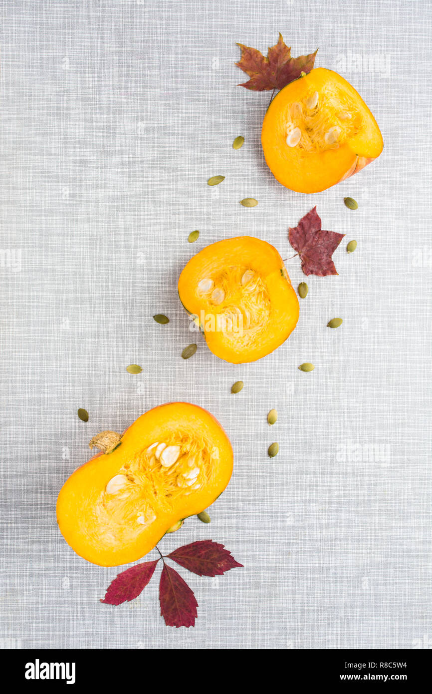 Overhead view of pumpkin parts with autumn leaves over grey background ...