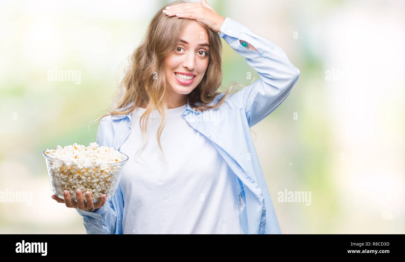Beautiful young blonde woman eating popcorn over isolated background ...