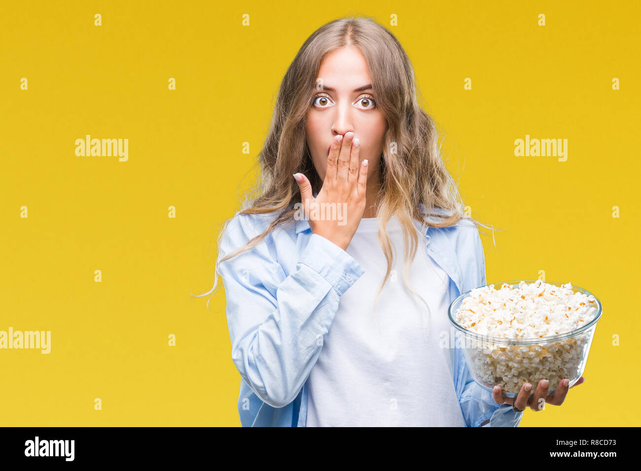 Beautiful young blonde woman eating popcorn over isolated background ...