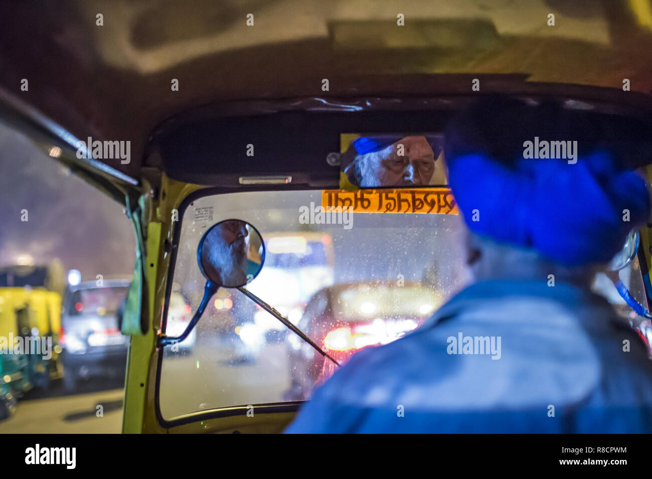 An auto-rickshaw driver is driving in the streets of New Delhi at night ...