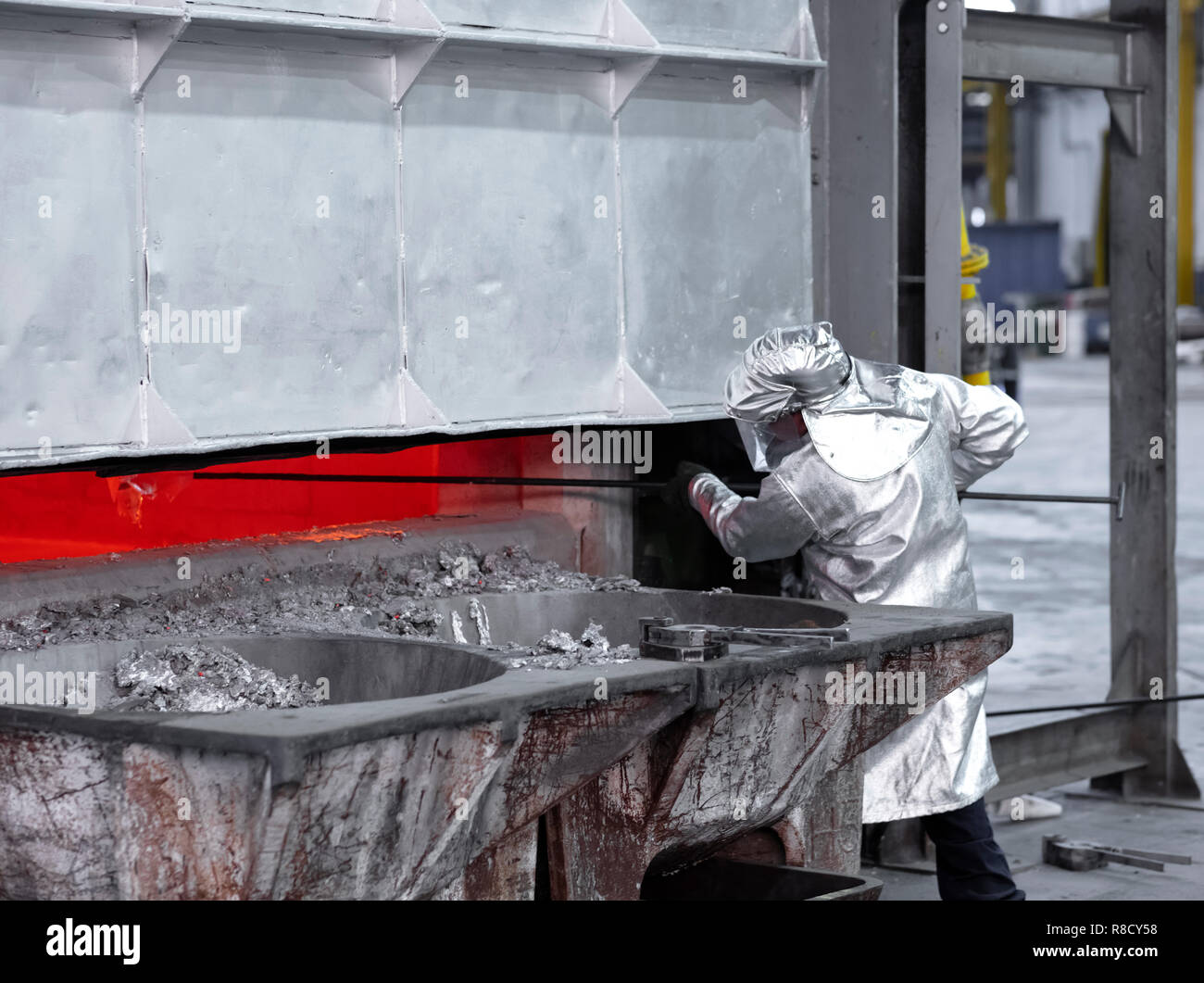 a worker taking a sample of molten aluminum from the inside of a big ...