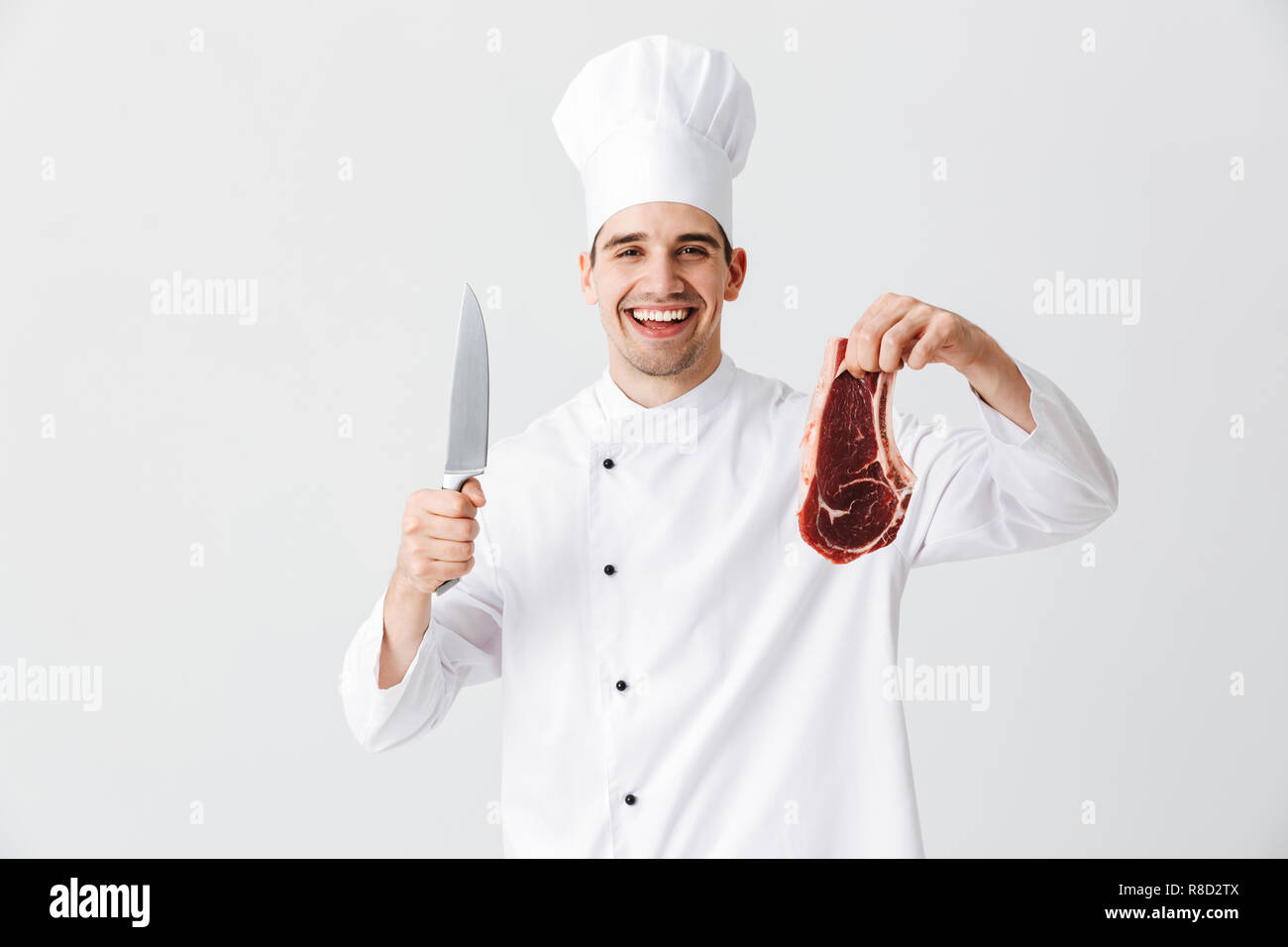 Cheerful chef cook wearing uniform showing raw beef steak holding a ...