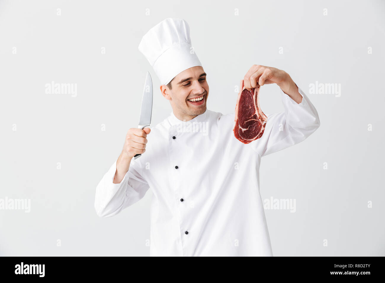 Cheerful chef cook wearing uniform showing raw beef steak holding a ...