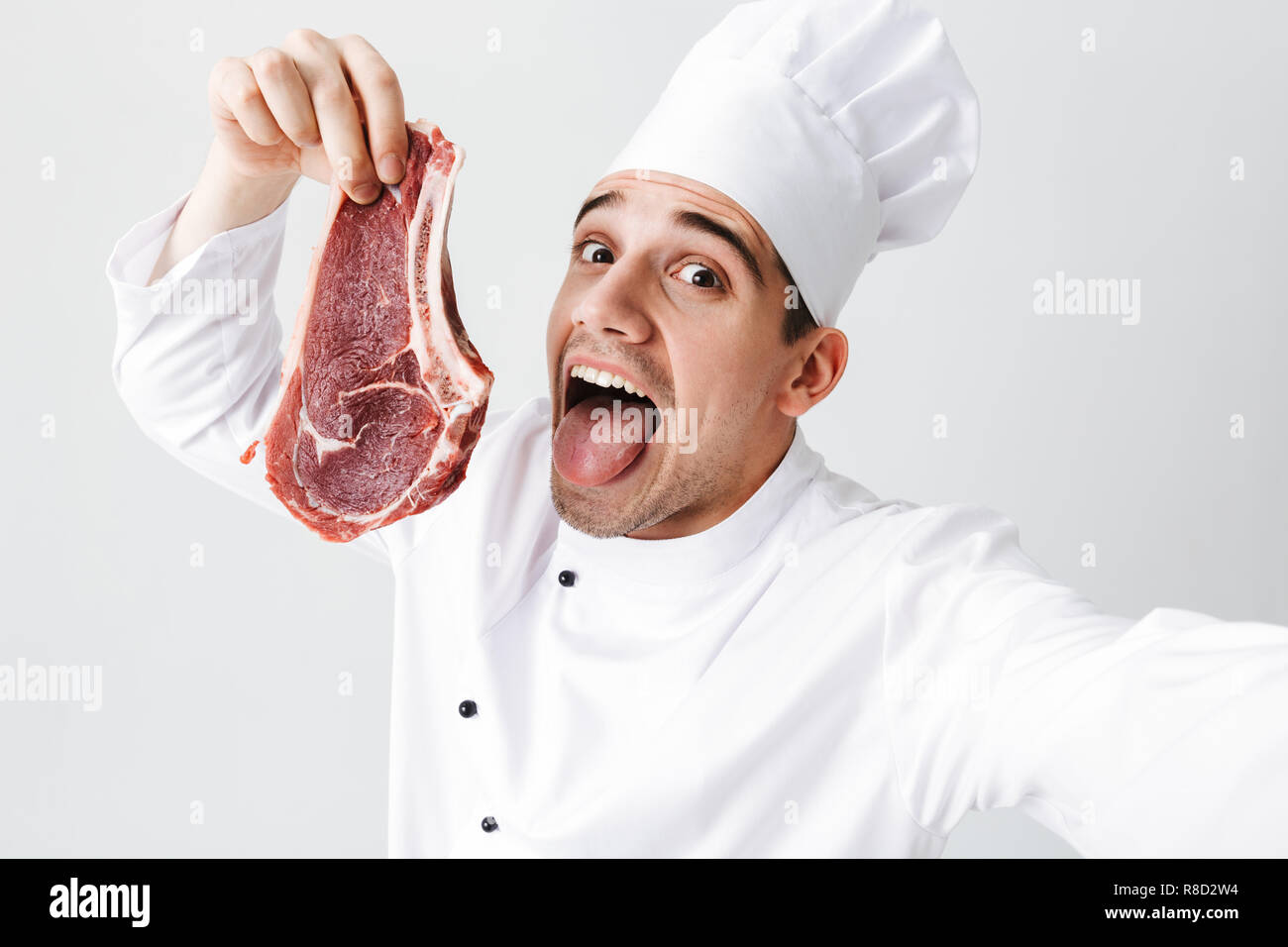 Cheerful chef cook wearing uniform showing raw beef steak isolated over ...
