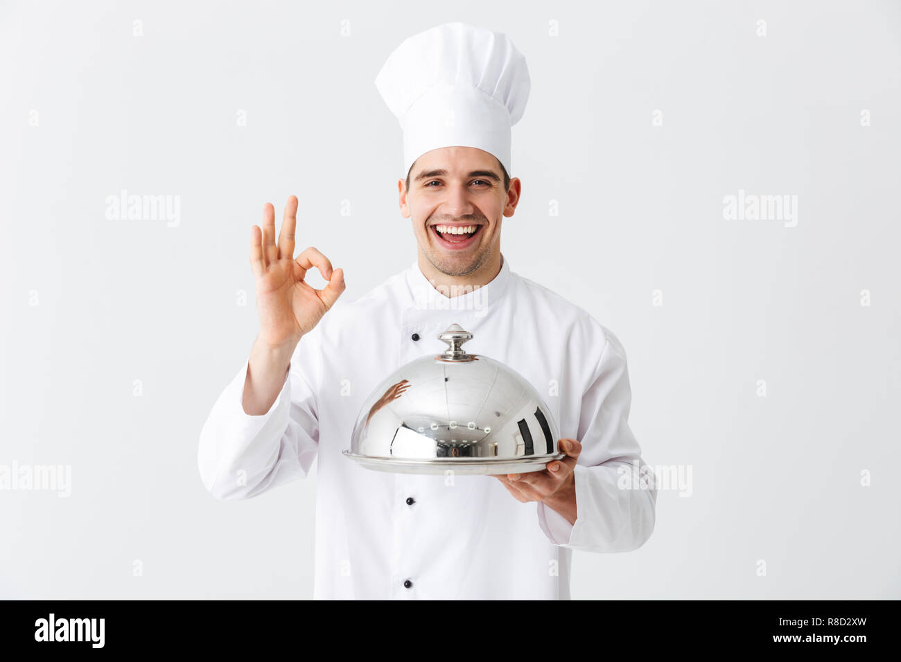 Excited man chef cook wearing uniform opening cloche cover isolated ...