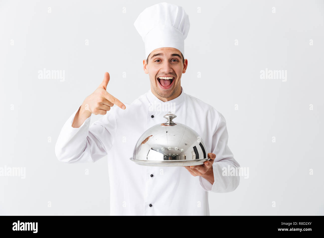 Excited man chef cook wearing uniform opening cloche cover isolated ...
