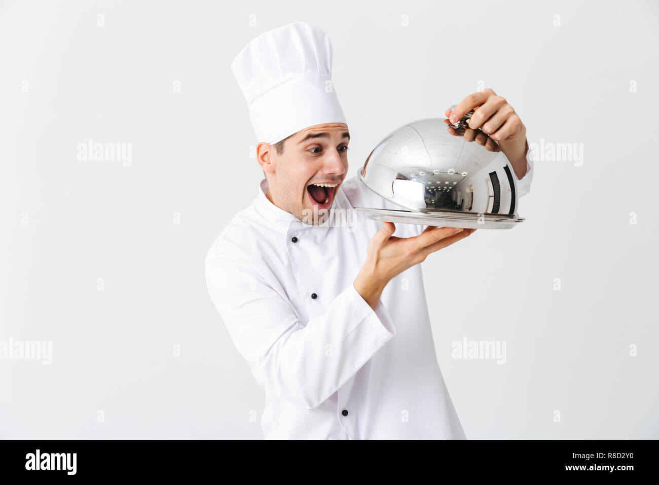 Excited man chef cook wearing uniform opening cloche cover isolated ...