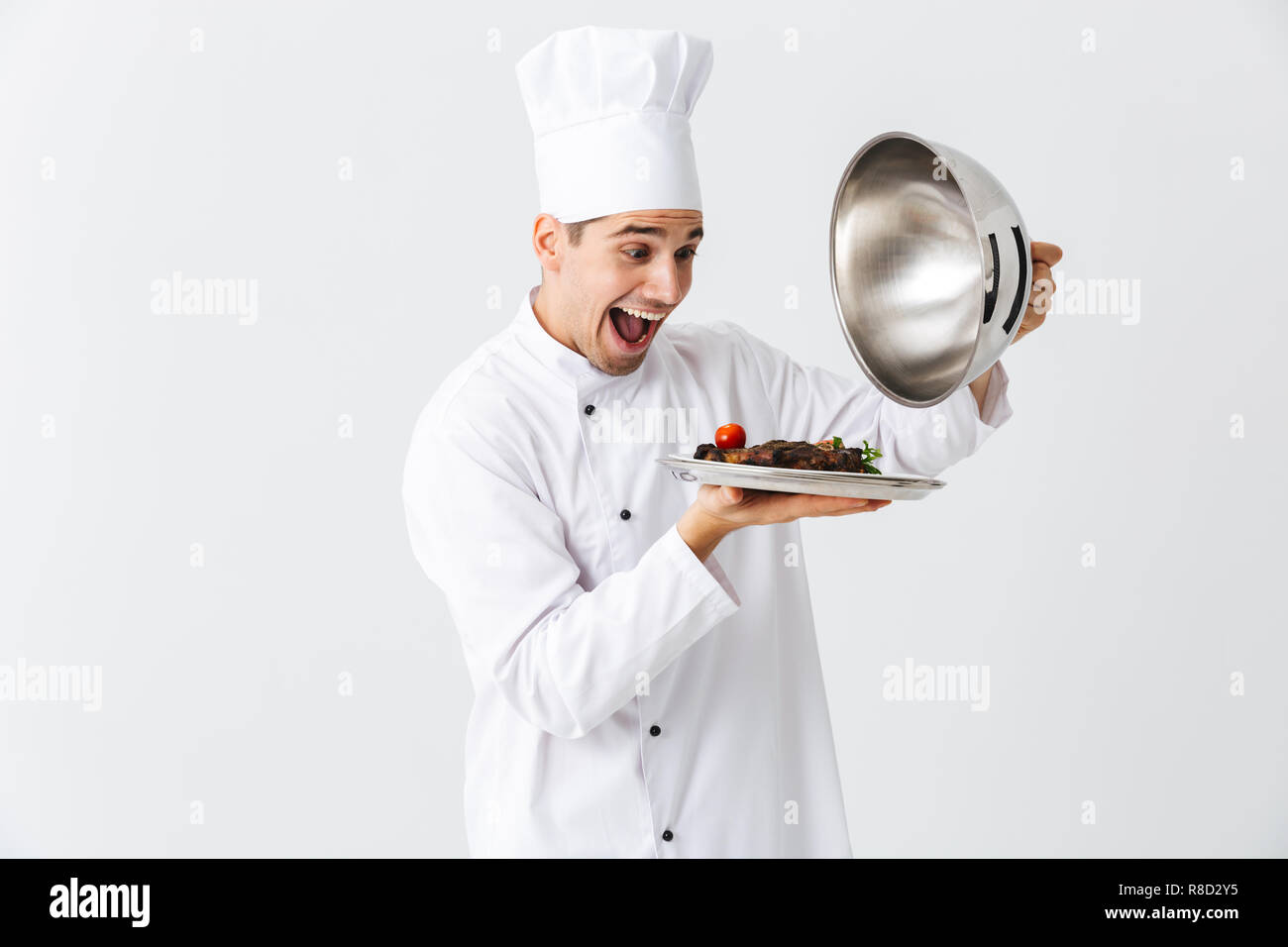 Excited man chef cook wearing uniform opening cloche cover isolated ...