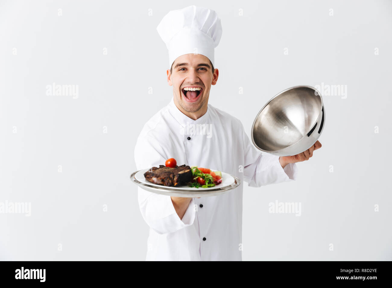 Excited man chef cook wearing uniform opening cloche cover isolated ...