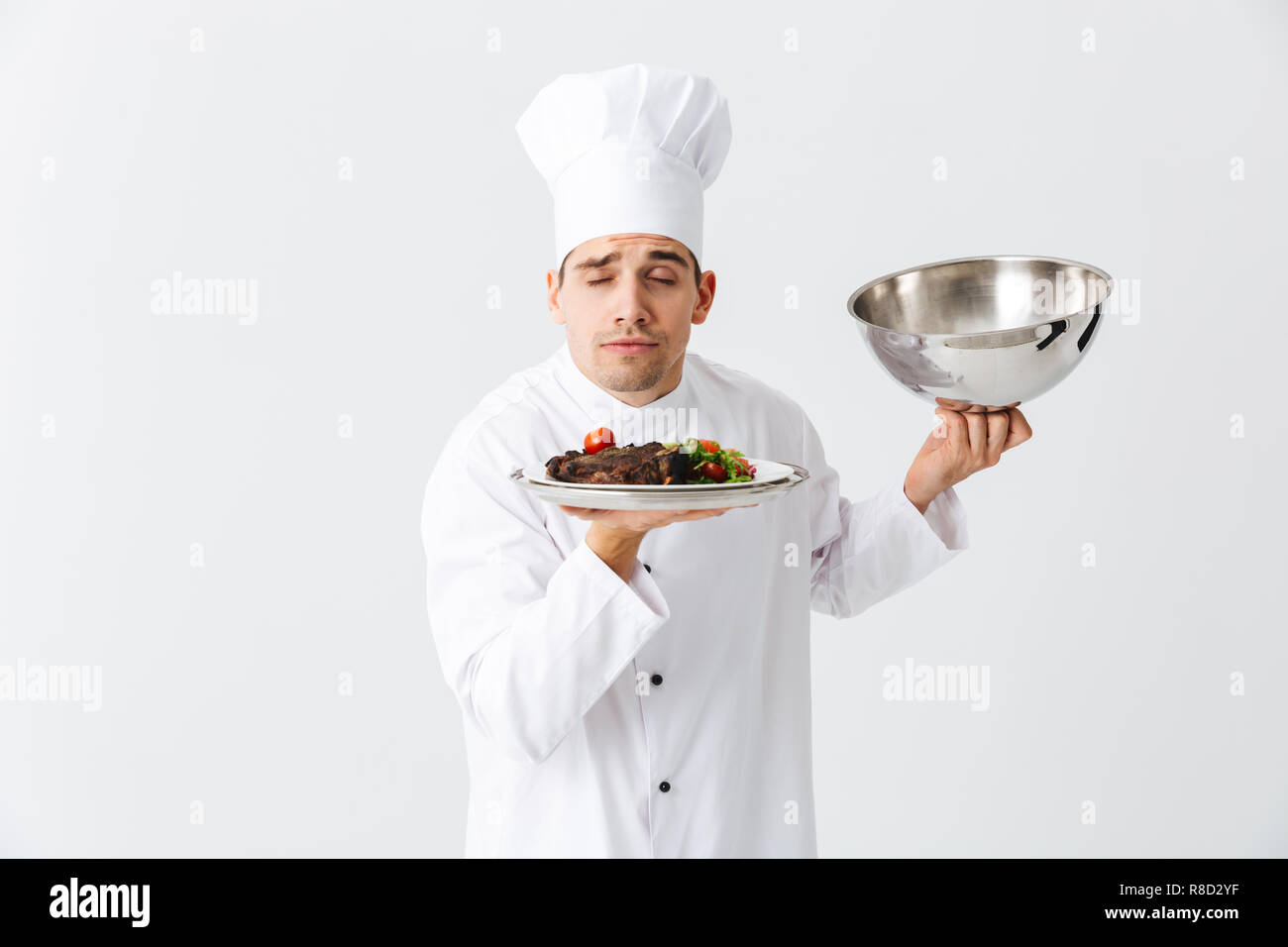 Excited man chef cook wearing uniform opening cloche cover isolated ...