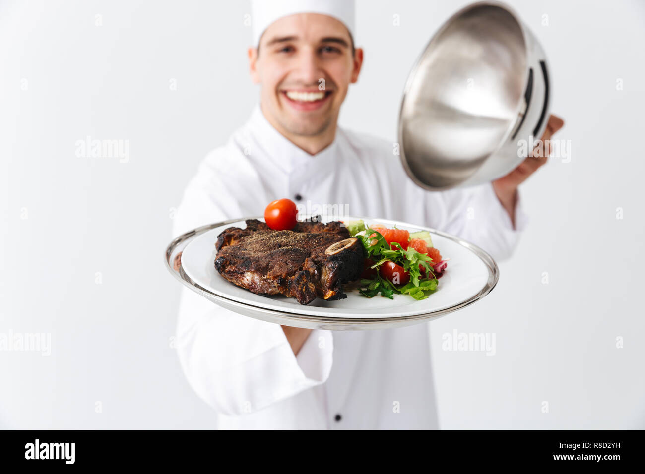 Excited man chef cook wearing uniform opening cloche cover isolated ...