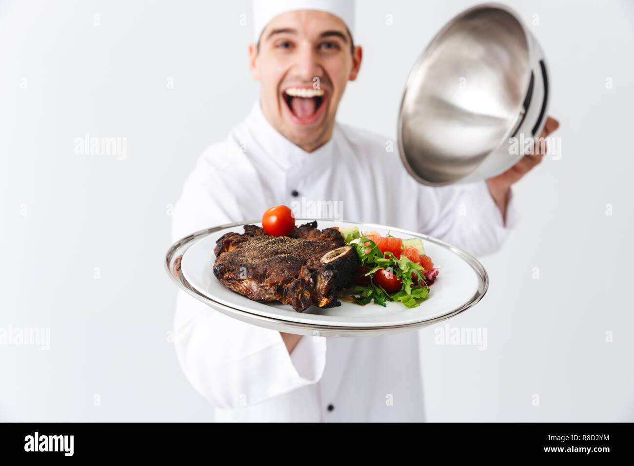 Excited man chef cook wearing uniform opening cloche cover isolated ...