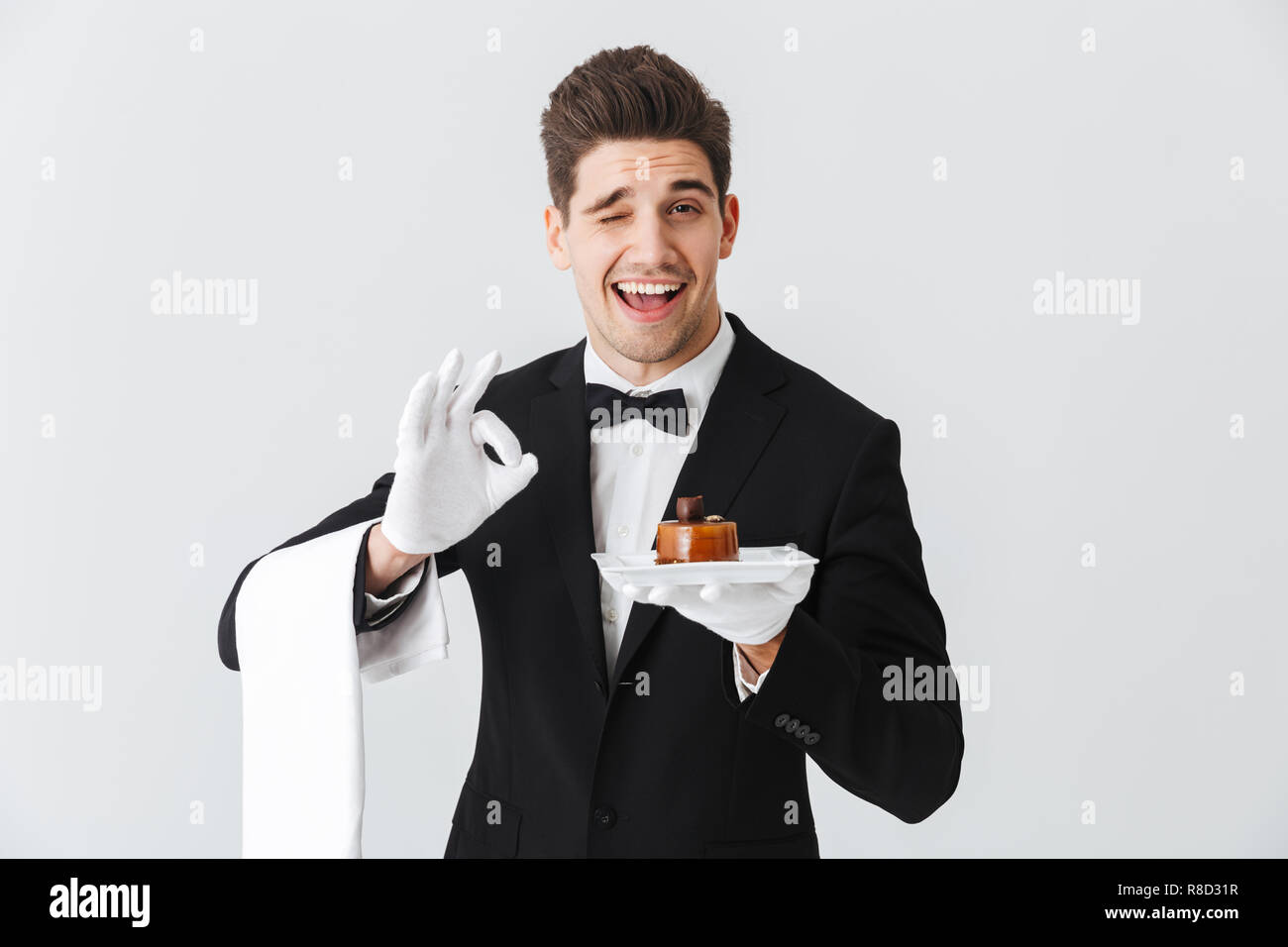 Handsome young waiter in tuxedo with bowtie holding plate with cake ...