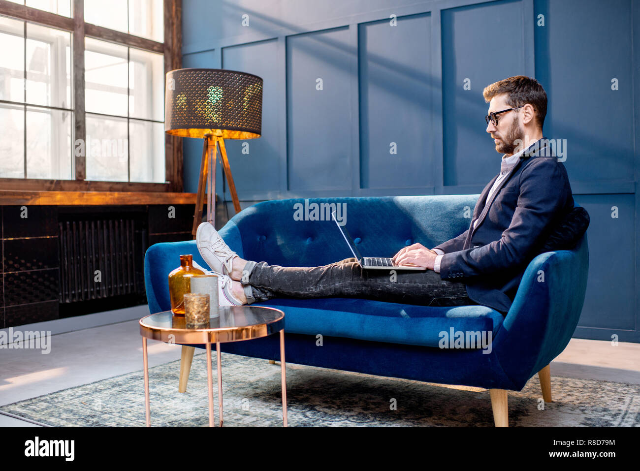 Portrait of an elegant businessman sitting with laptop on the couch at ...