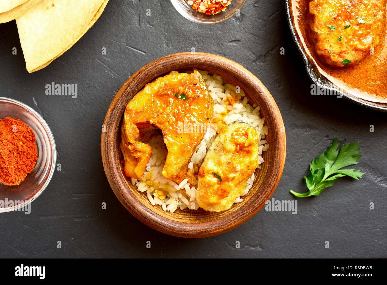 Indian style fish curry with rice in wooden bowl on black stone table ...