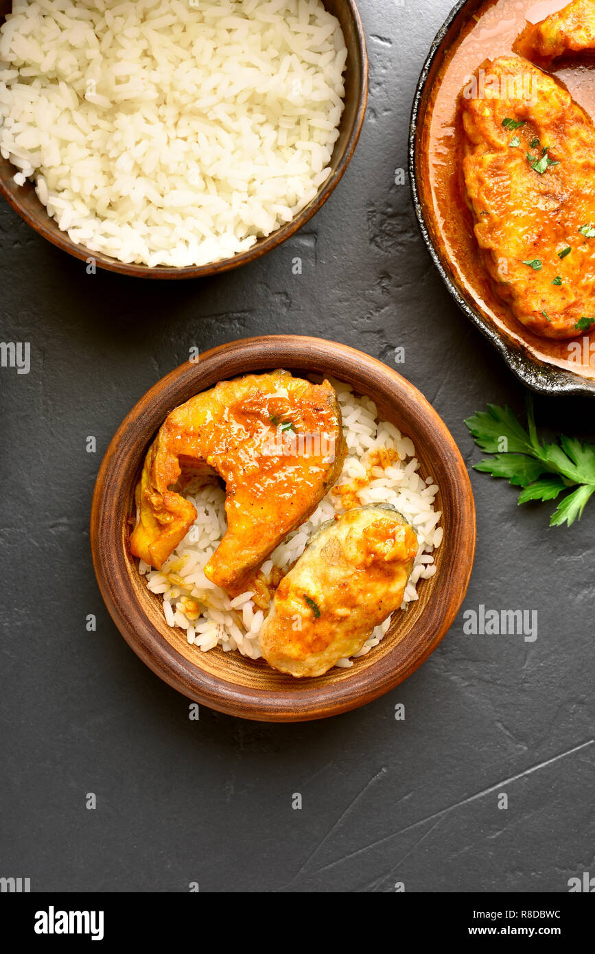 Delicious fish curry with rice in wooden bowl on black stone background ...