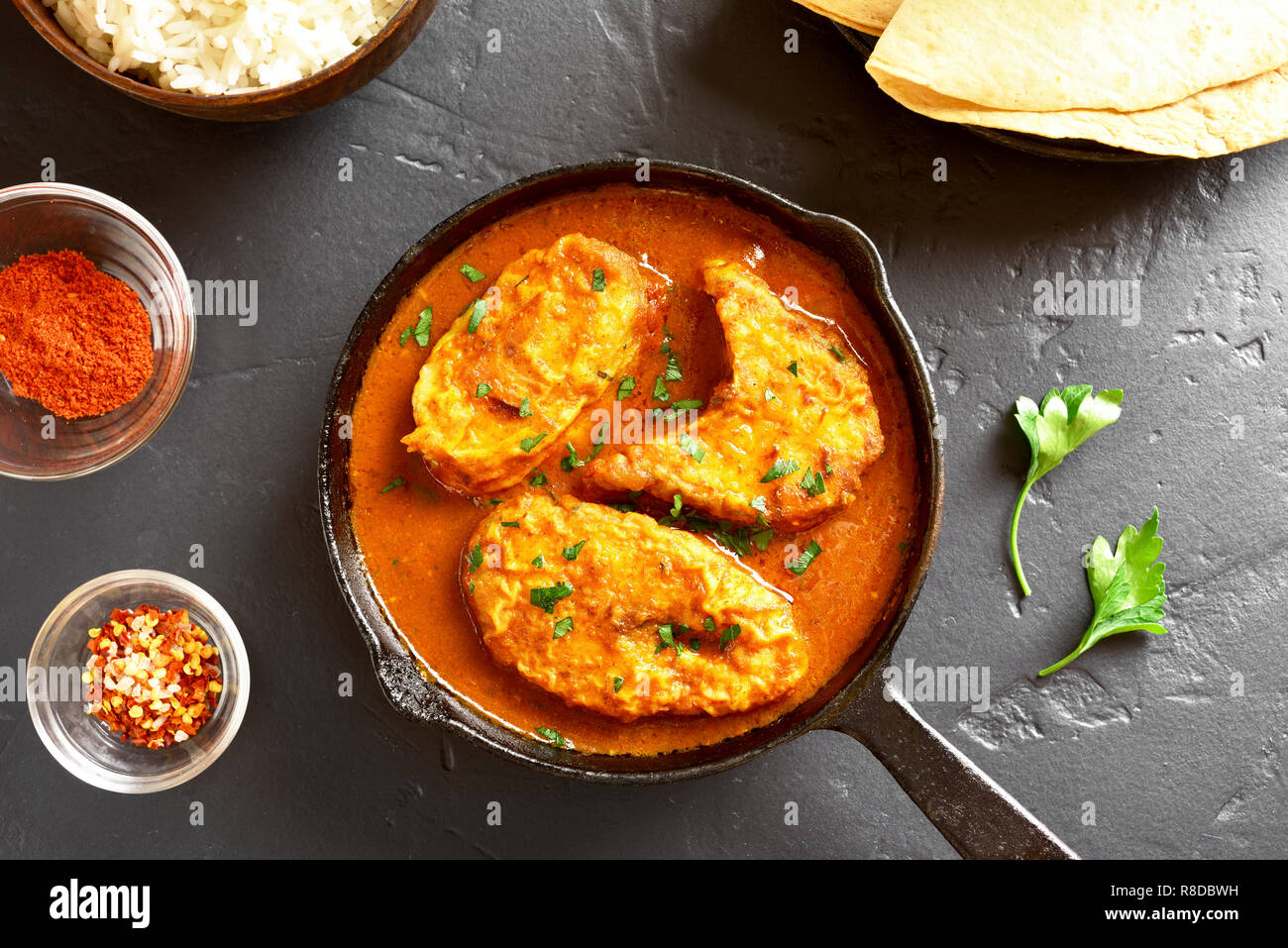 Close up of fish curry in frying pan on black stone table. Indian style ...