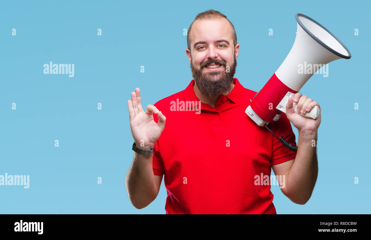 Young caucasian man shouting through megaphone over isolated background ...