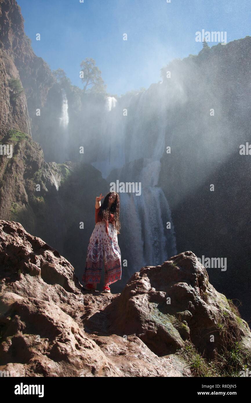 A young, hippie female tourist poses in front of a dramatic waterfall ...