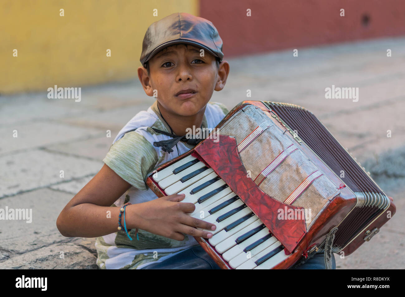Isolated shot of a young Oaxacan boy in a hat, sitting on a stone curb ...