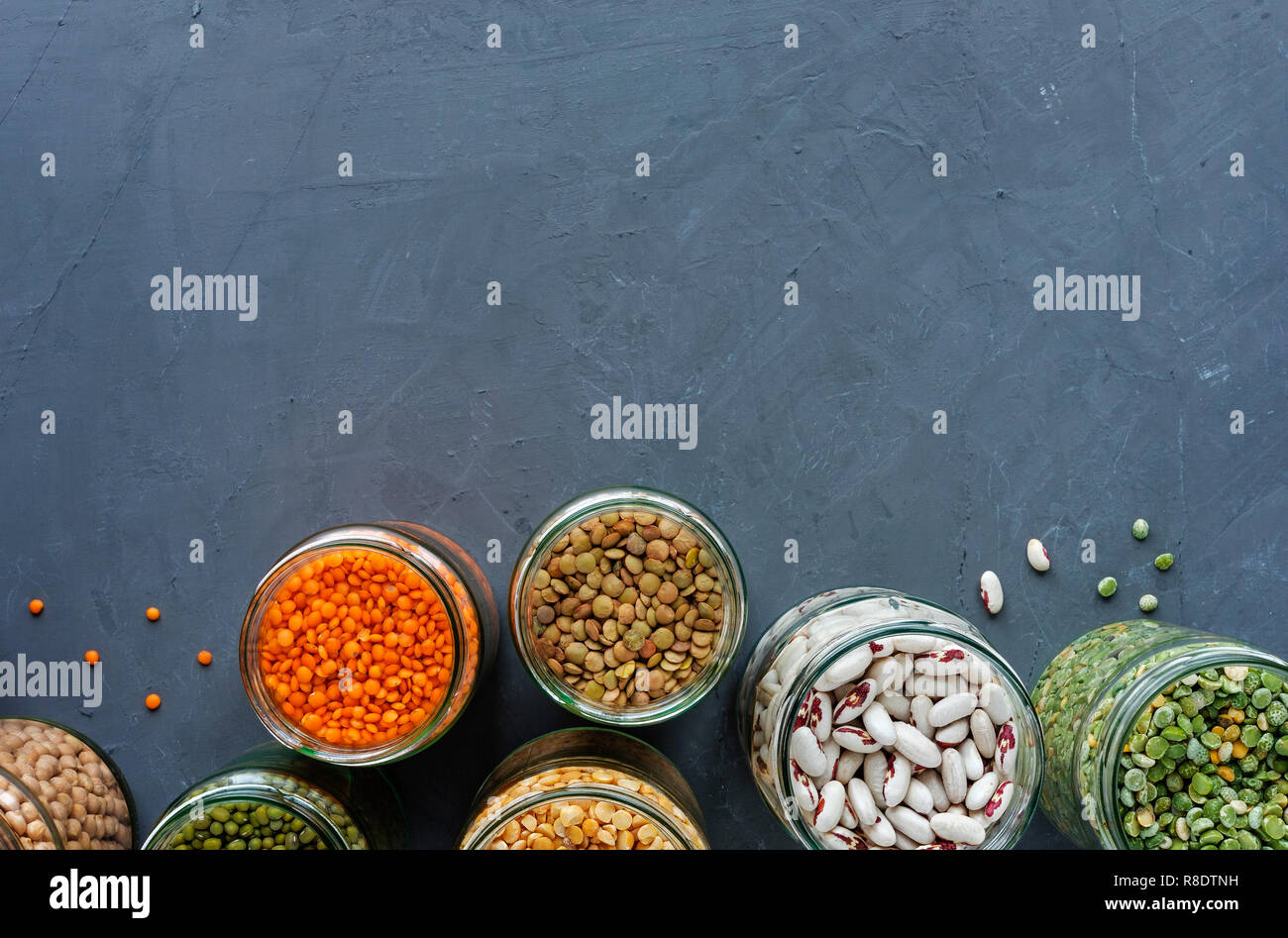 Dried legumes in storage jars on mottled blue background viewed from ...