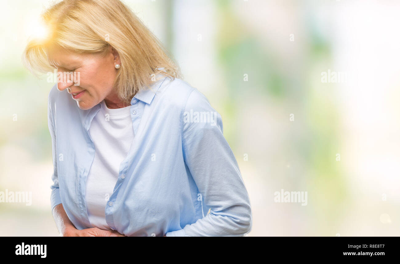 Middle age blonde woman over isolated background with hand on stomach because nausea, painful ...