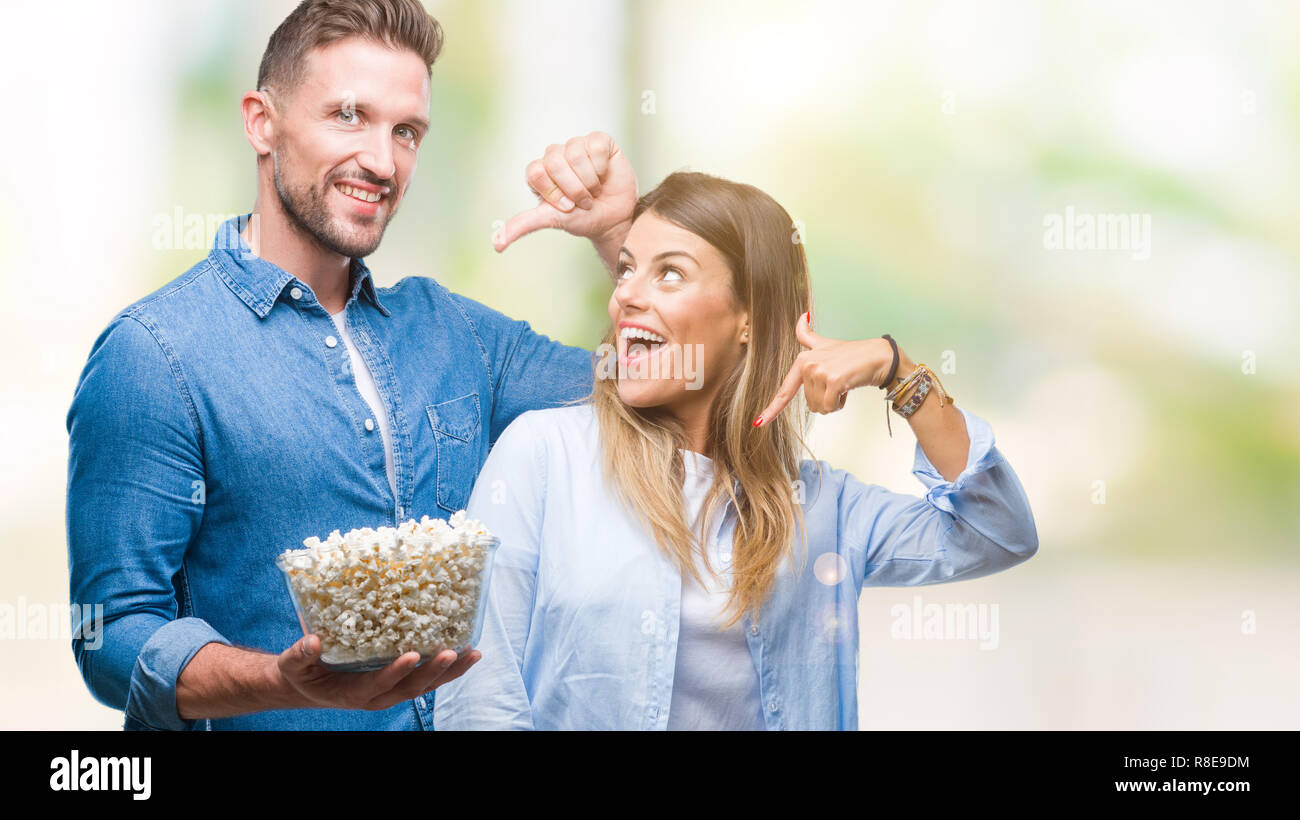 Young couple in love eating popcorn over isolated background with ...