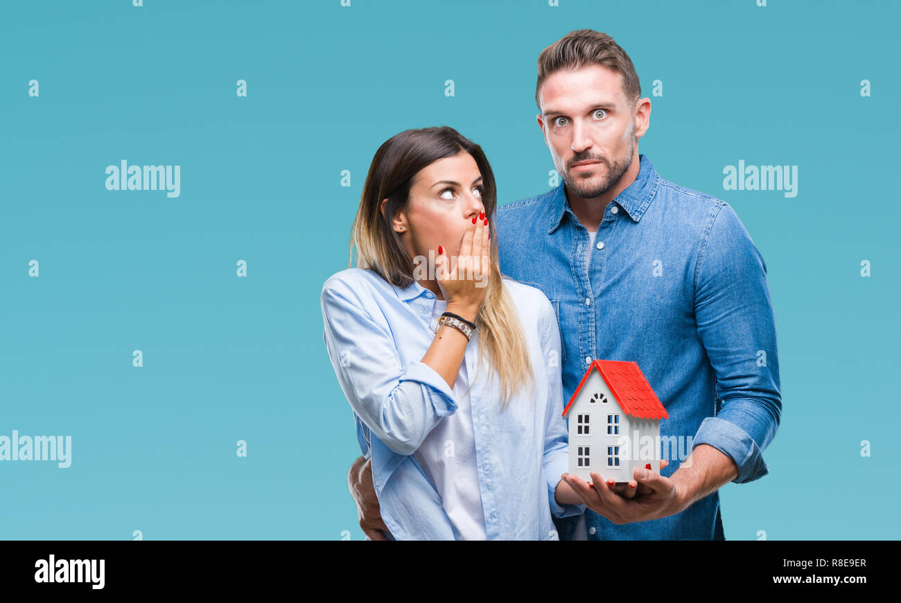 Young couple in love holding house over isolated background cover mouth ...