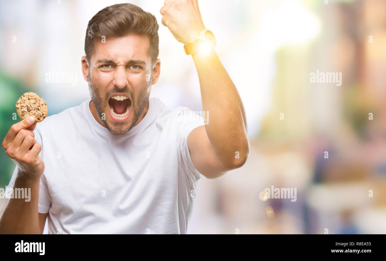 Young handsome man eating chocolate chips cookie over isolated ...