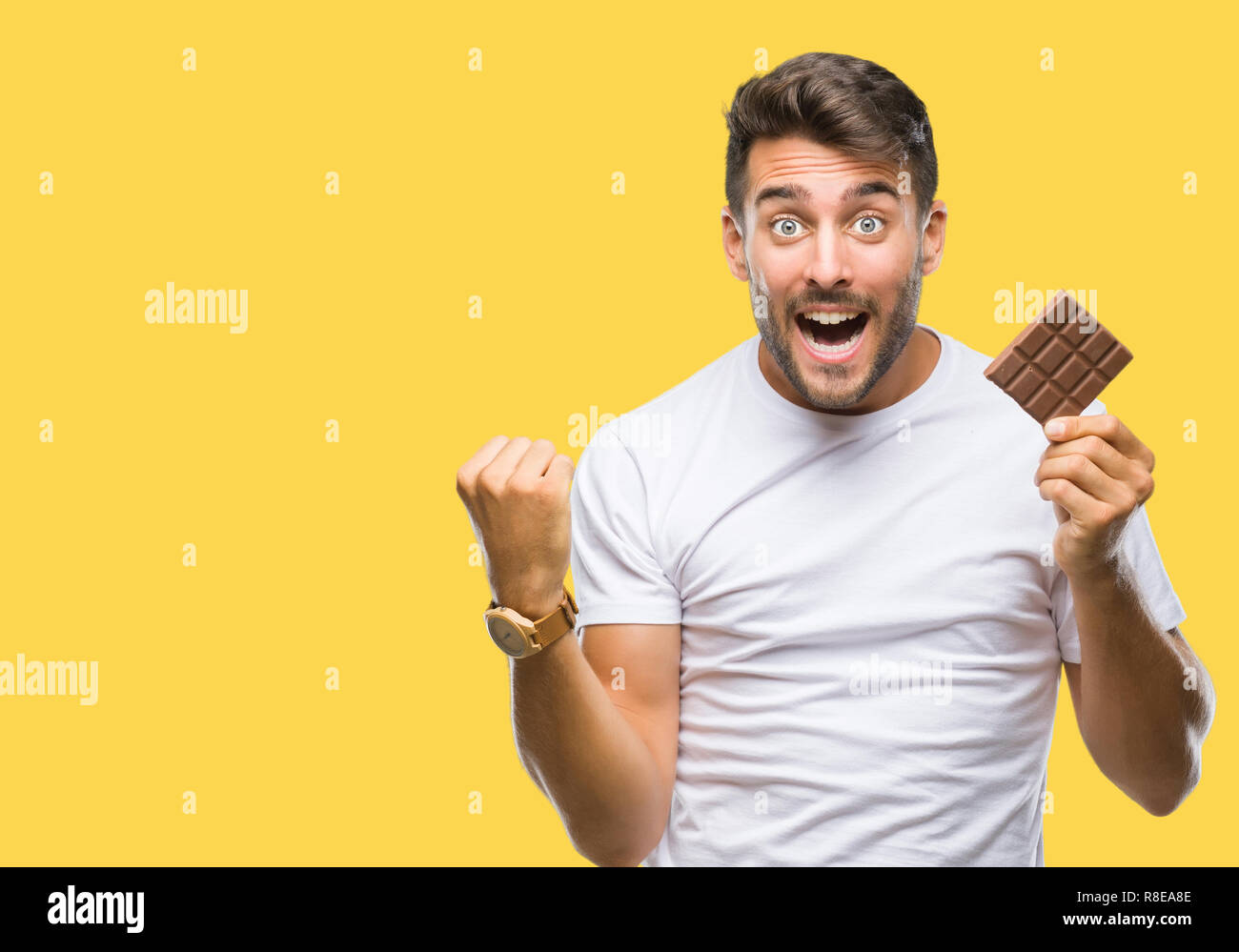 Young handsome man eating chocolate bar over isolated background ...