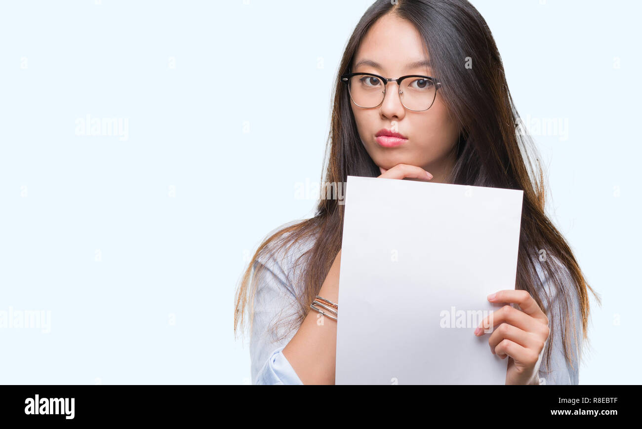 Young asian woman holding blank paper over isolated background serious ...