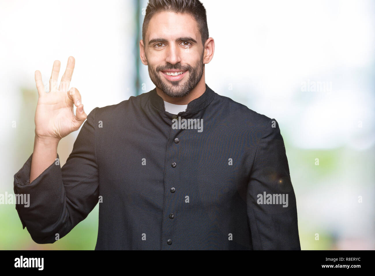 Young Christian priest over isolated background smiling positive doing ...