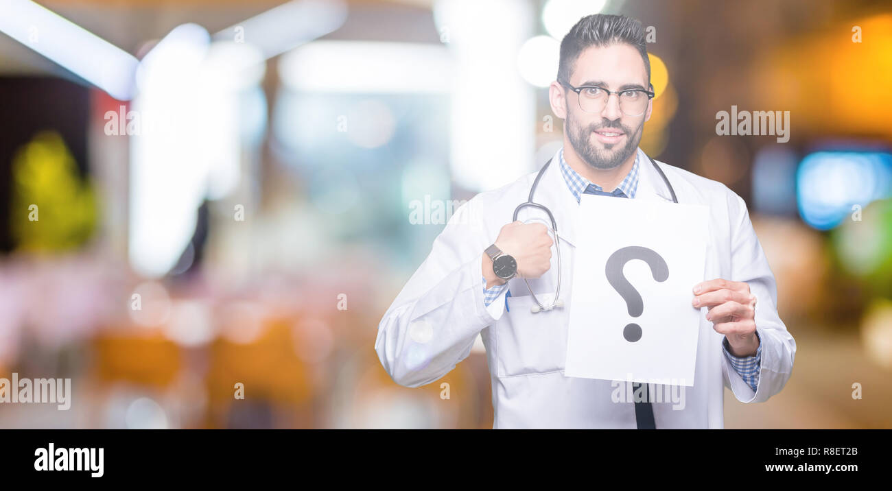 Handsome young doctor man holding paper with question mark over ...