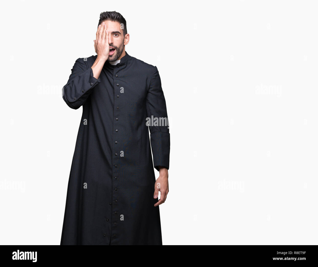 Young Christian priest over isolated background covering one eye with ...