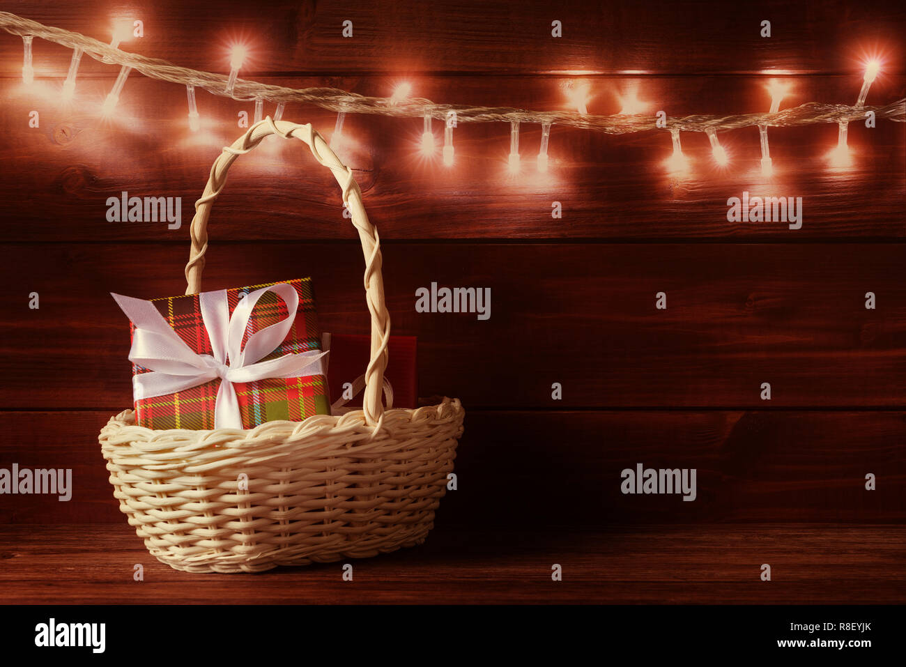 Gift boxes in basket over glowing garland Stock Photo - Alamy