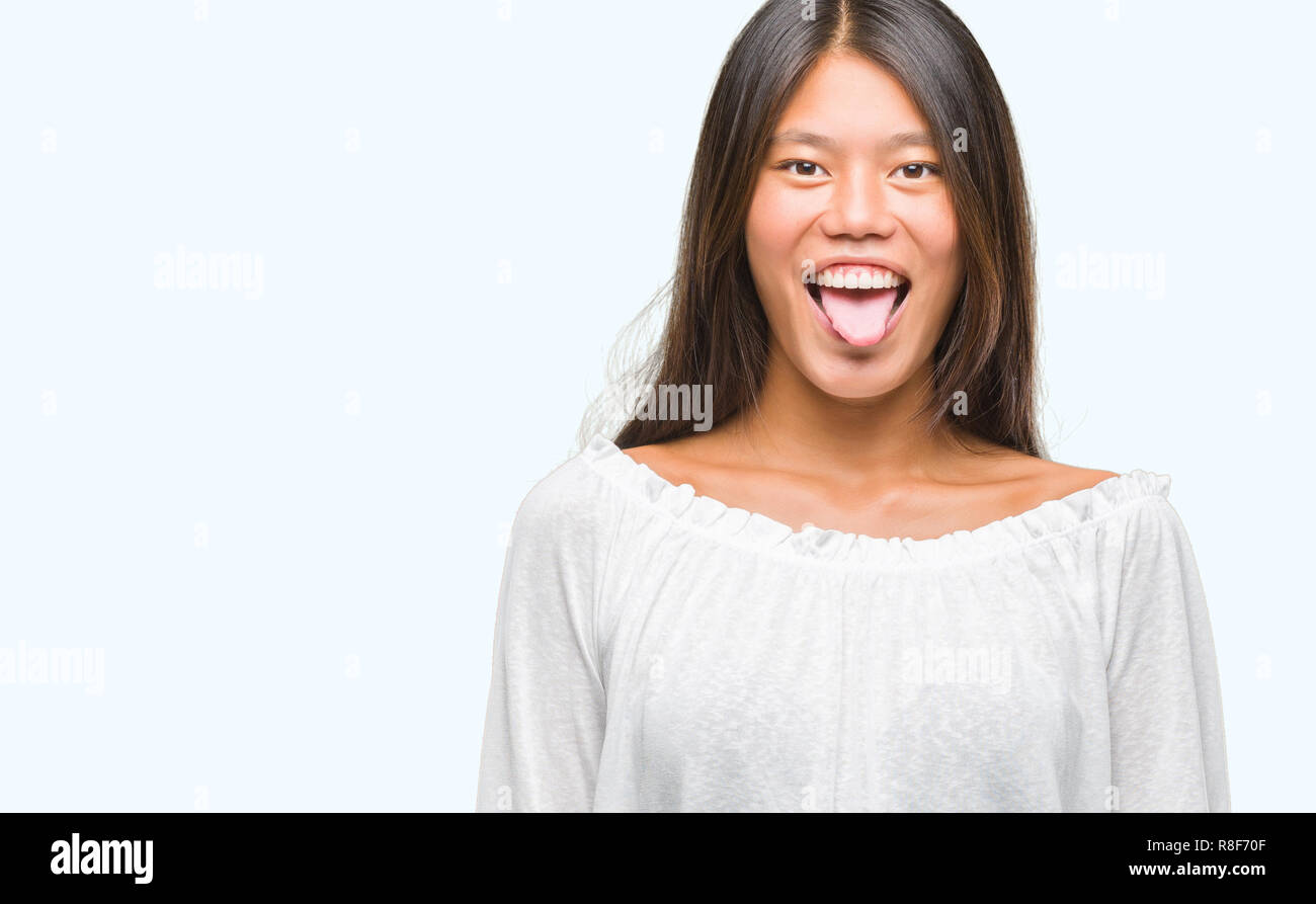 Young asian woman over isolated background sticking tongue out happy ...