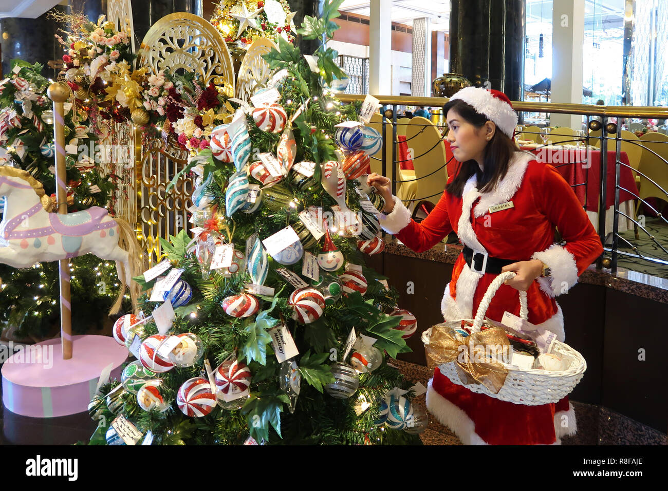 A young Filipino woman in Santa Claus outfit decorates a Christmas tree ...