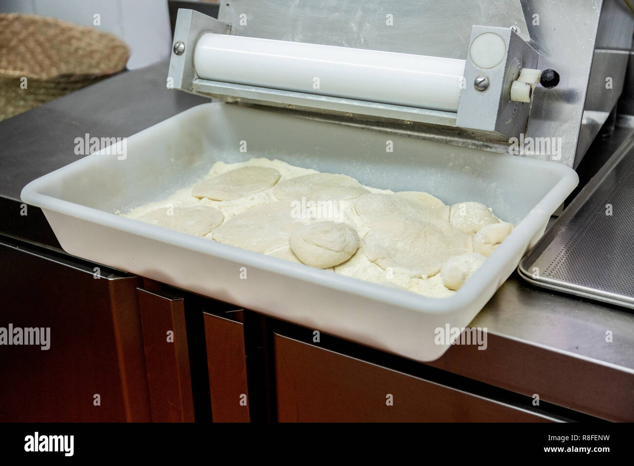 a tray in a restaurant kitchen with raw mass and flour and a roller pin ...