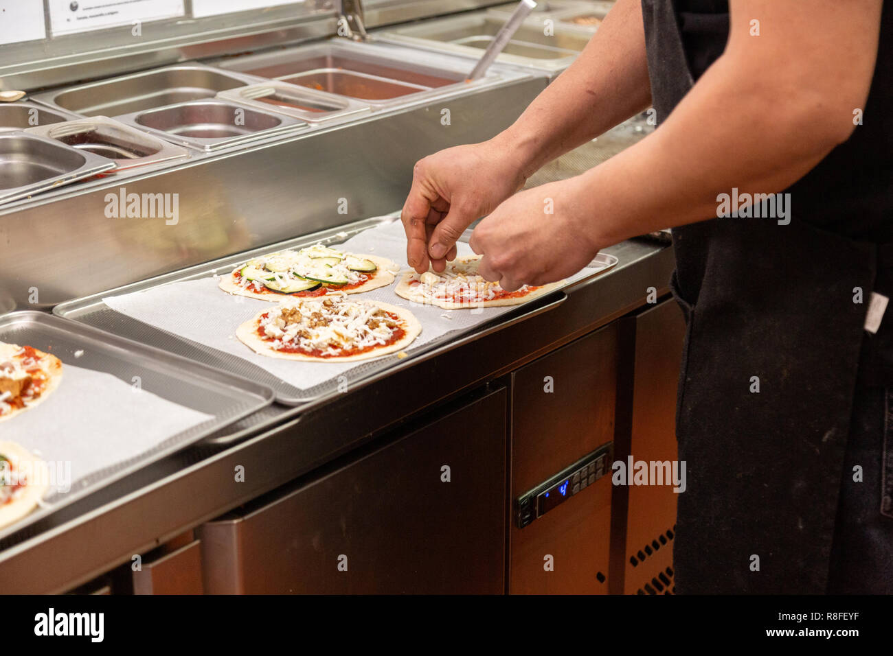 Chef hands adding ingredients on a pizza on a restaurant kitchen in a ...