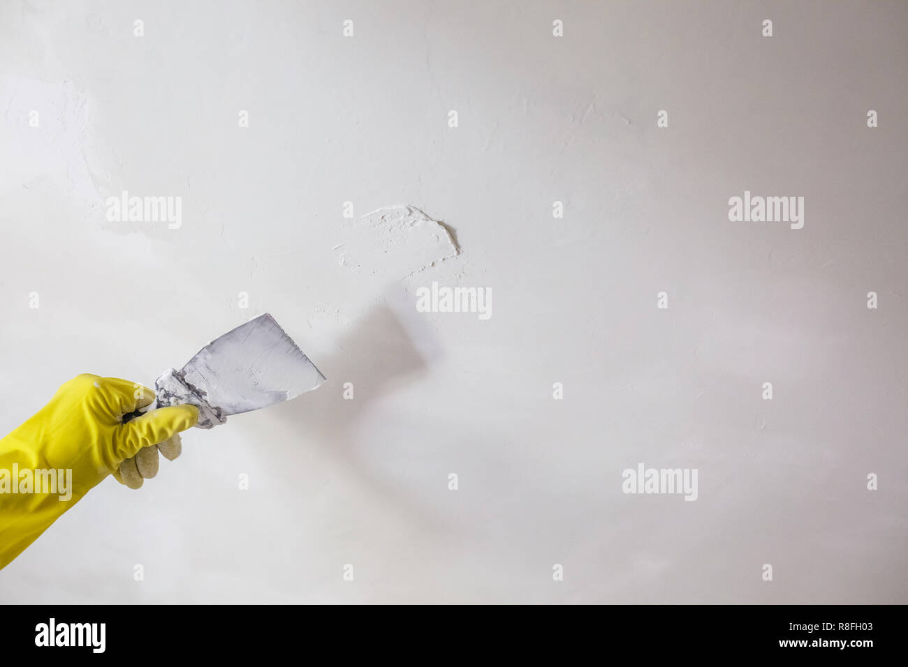 worker's hand in yellow gloves holding putty knife patching a hole with ...