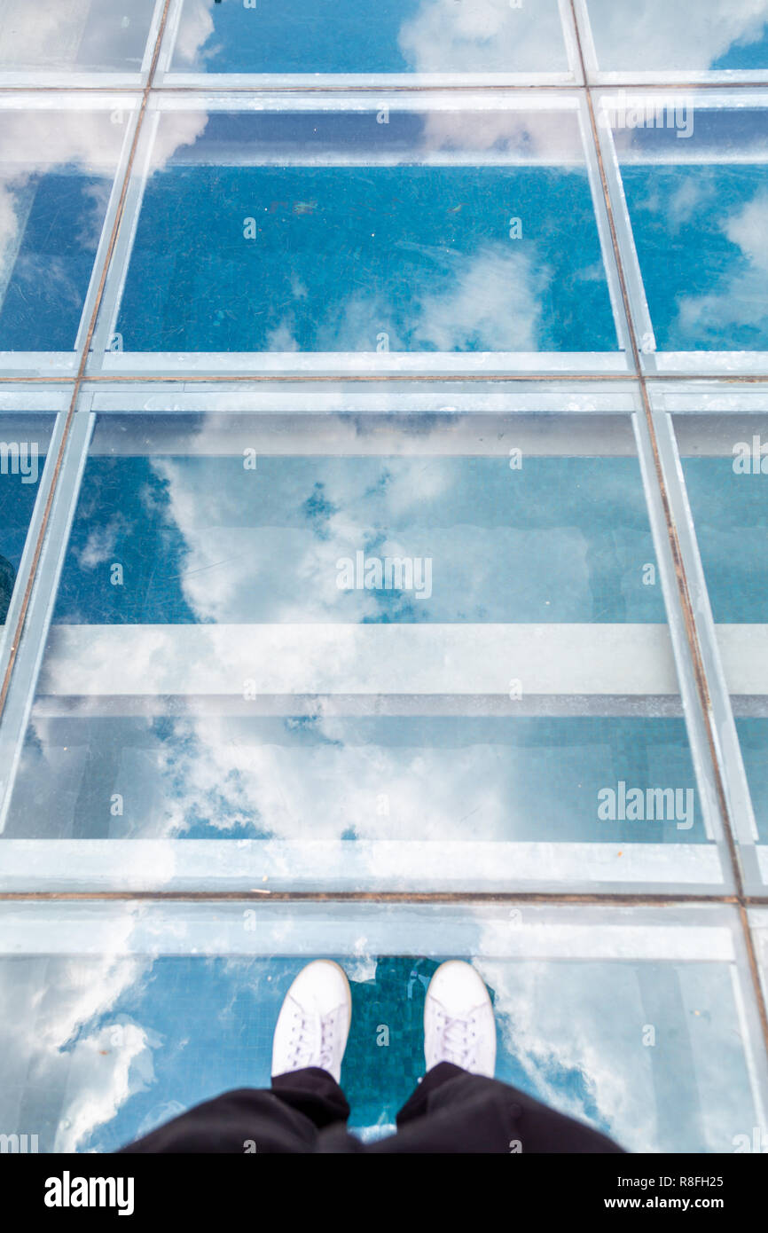 feet standing on the reflection in the floor of the blue sky with white ...