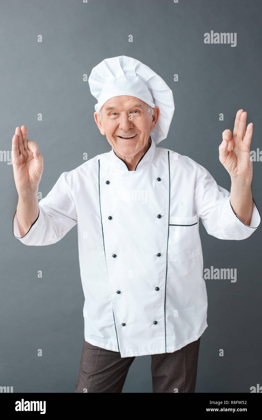 Senior chef studio standing isolated on gray smiling cheerful showing ...
