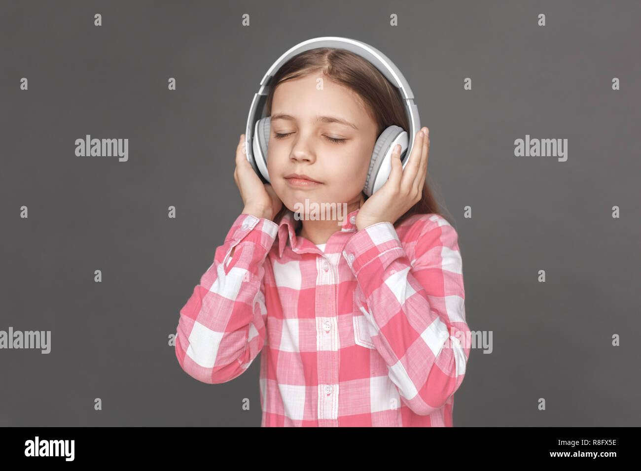 Freestyle. Girl in headphones standing isolated on grey listening to ...