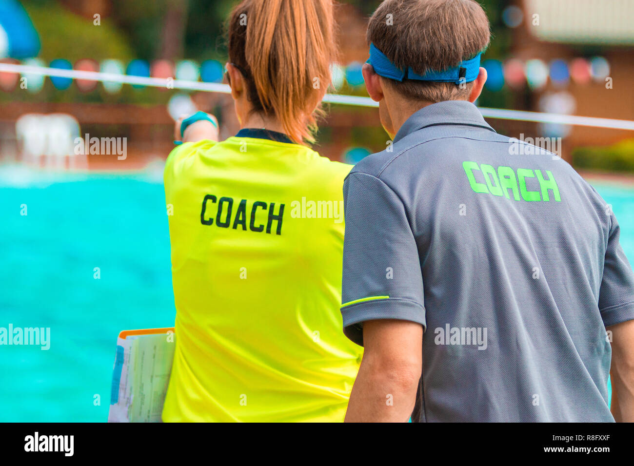 Back View Of Swimming Coaches Wearing Coach Shirt Working Together At