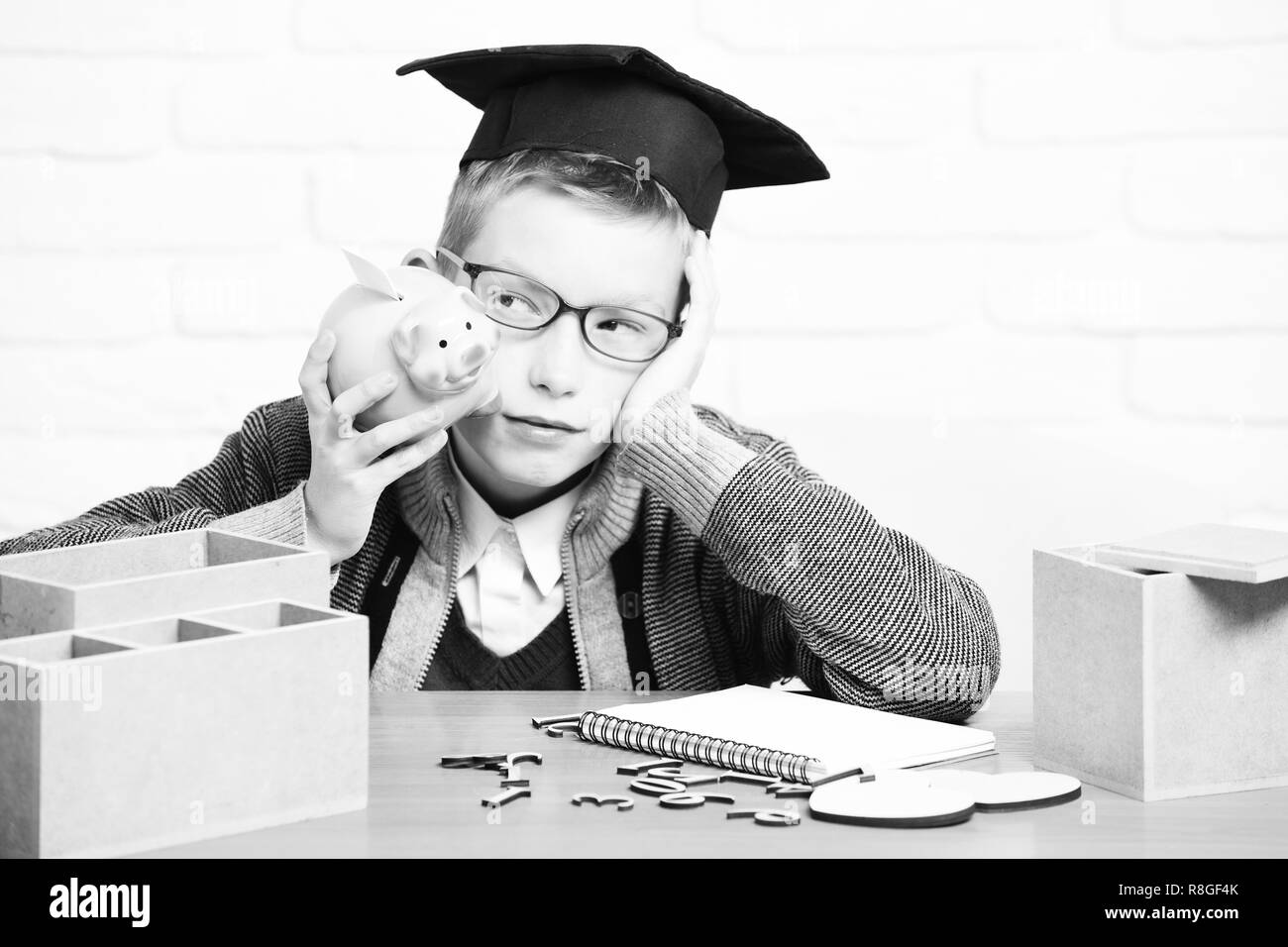 young cute pupil boy in grey sweater and glasses sitting at desk ...