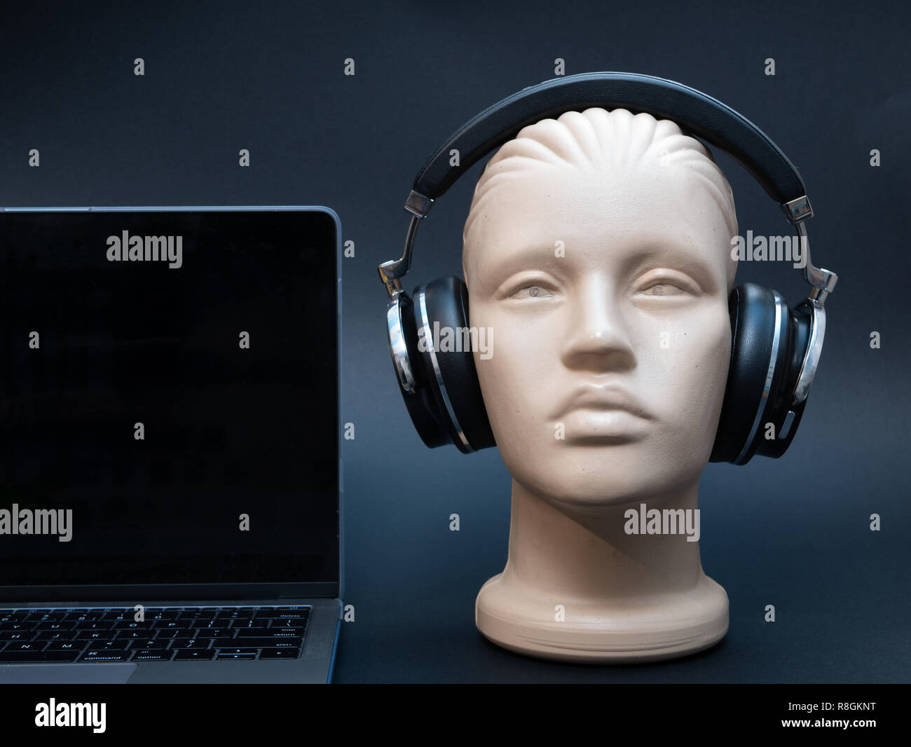 dummy head with over head headphones and laptop on dark black ...