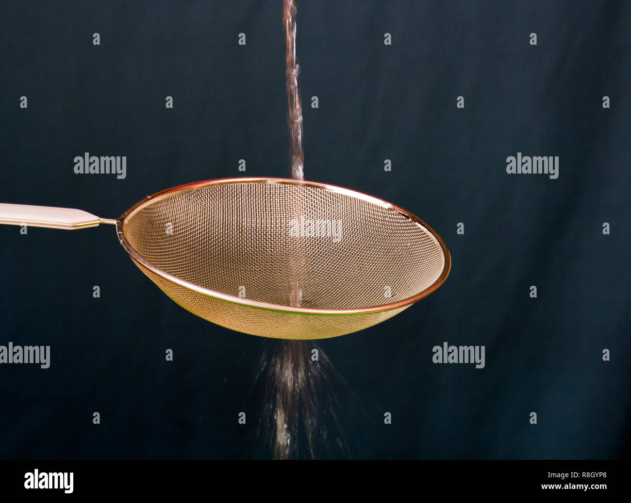 A stream of water pouring through a metal sieve isolated on a clear ...