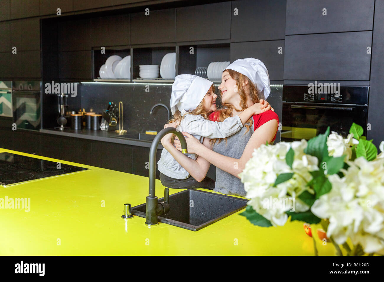 Two girls with chef hat hugging and having fun in kitchen. Sisters ...