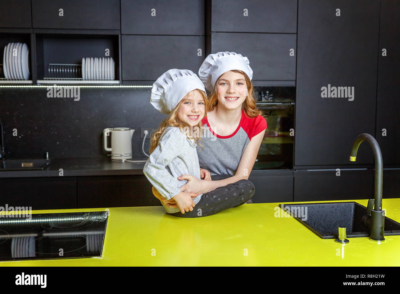 Two girls with chef hat hugging and having fun in kitchen. Sisters ...