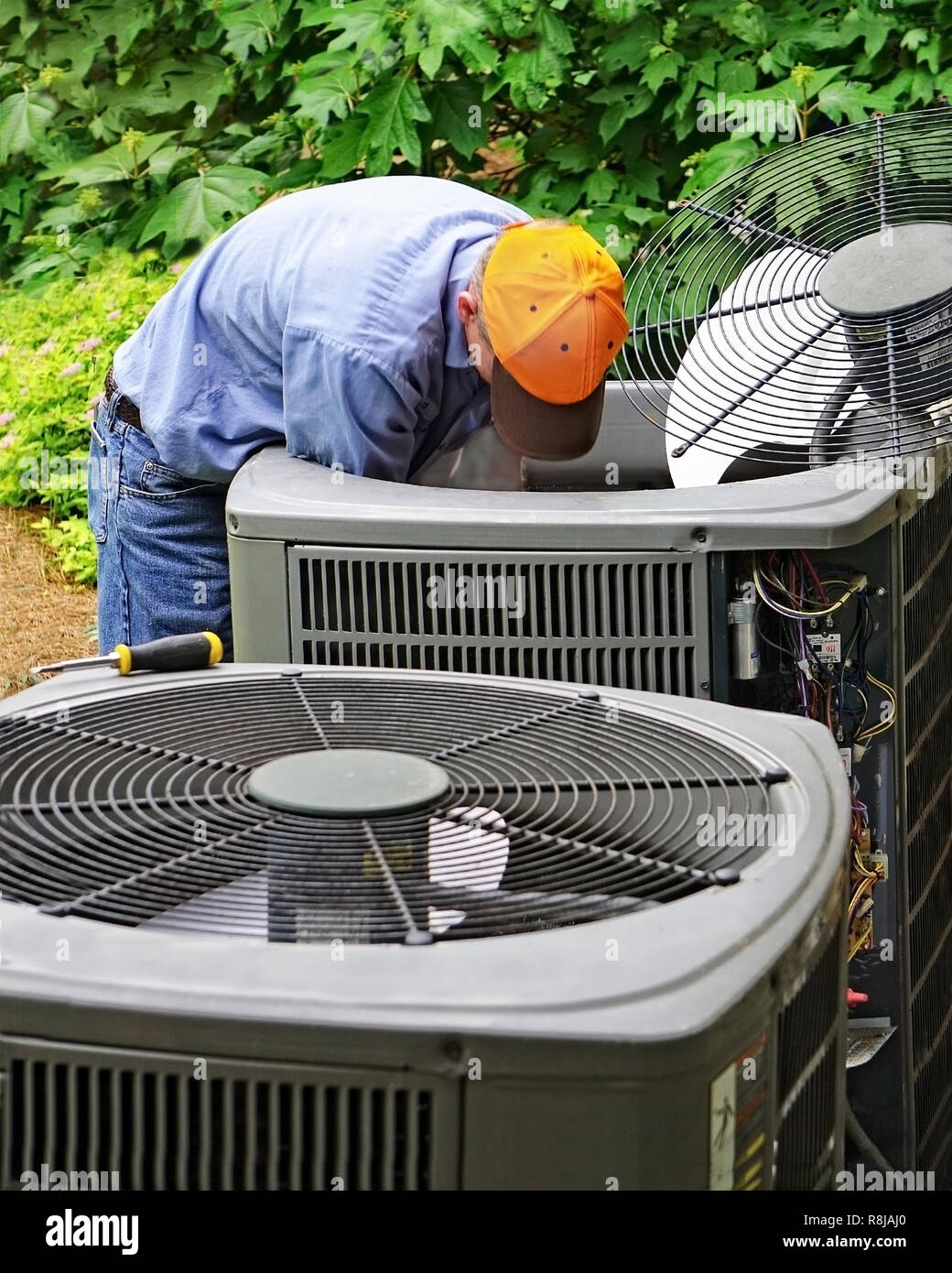 Repairman working on an air conditioner unit at the back of a house ...